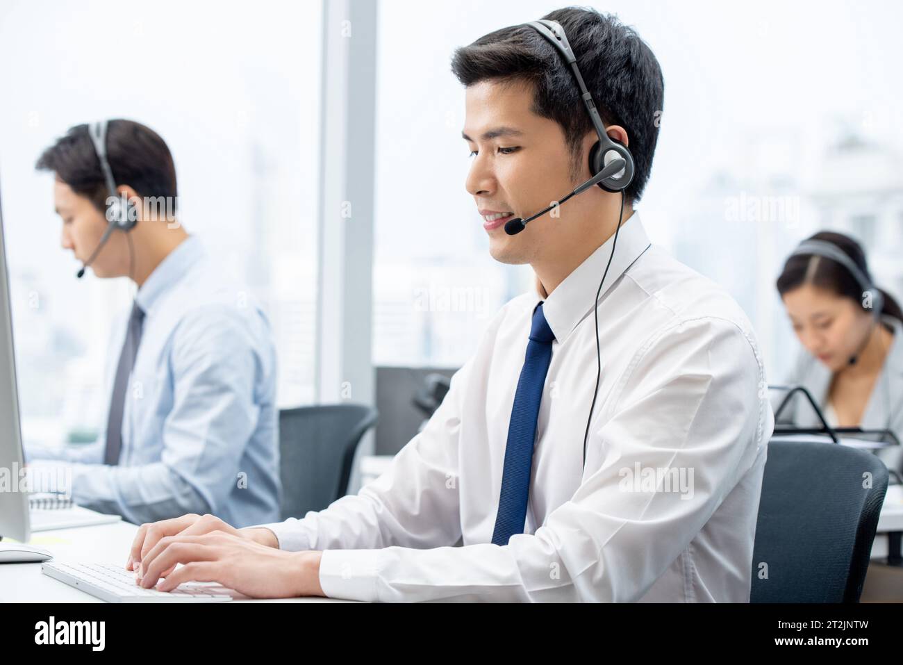 Side view of focused Asian male worker in headset typing on computer ...