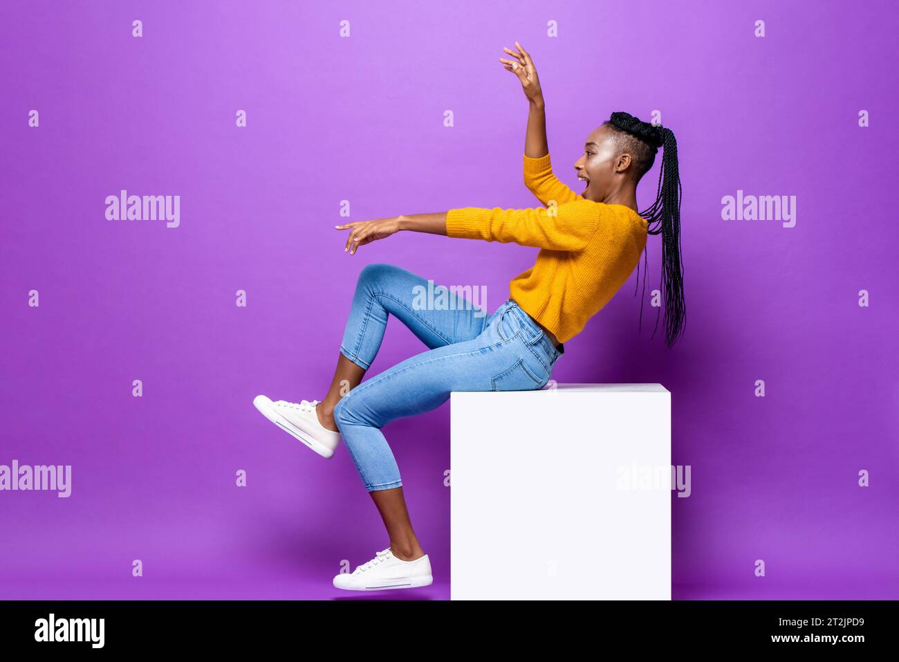 Fun excited young African-American woman sitting on stool raising leg ...