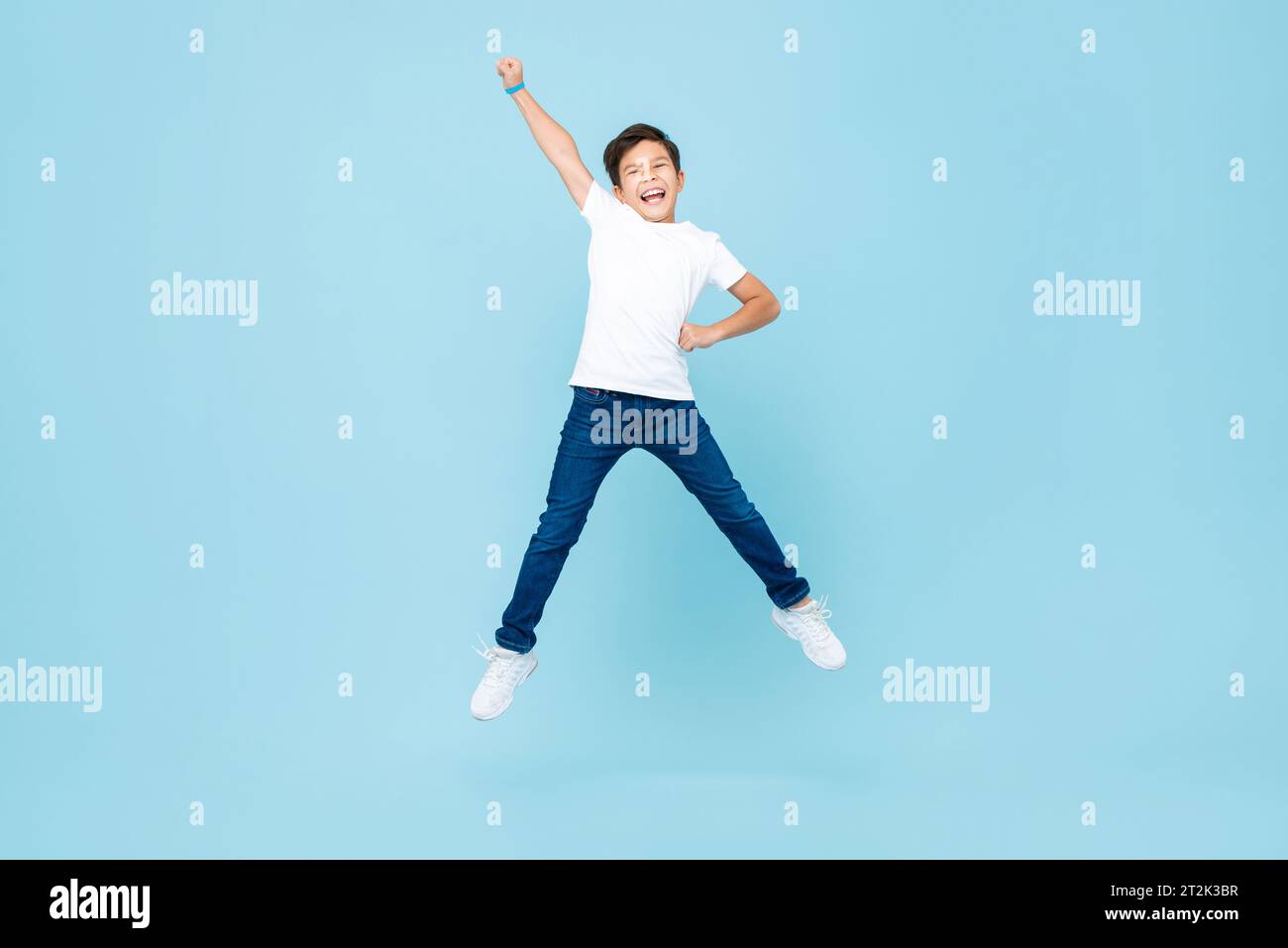 Cheerful Asian mixed race boy jumping and raising hand up in isolated ...