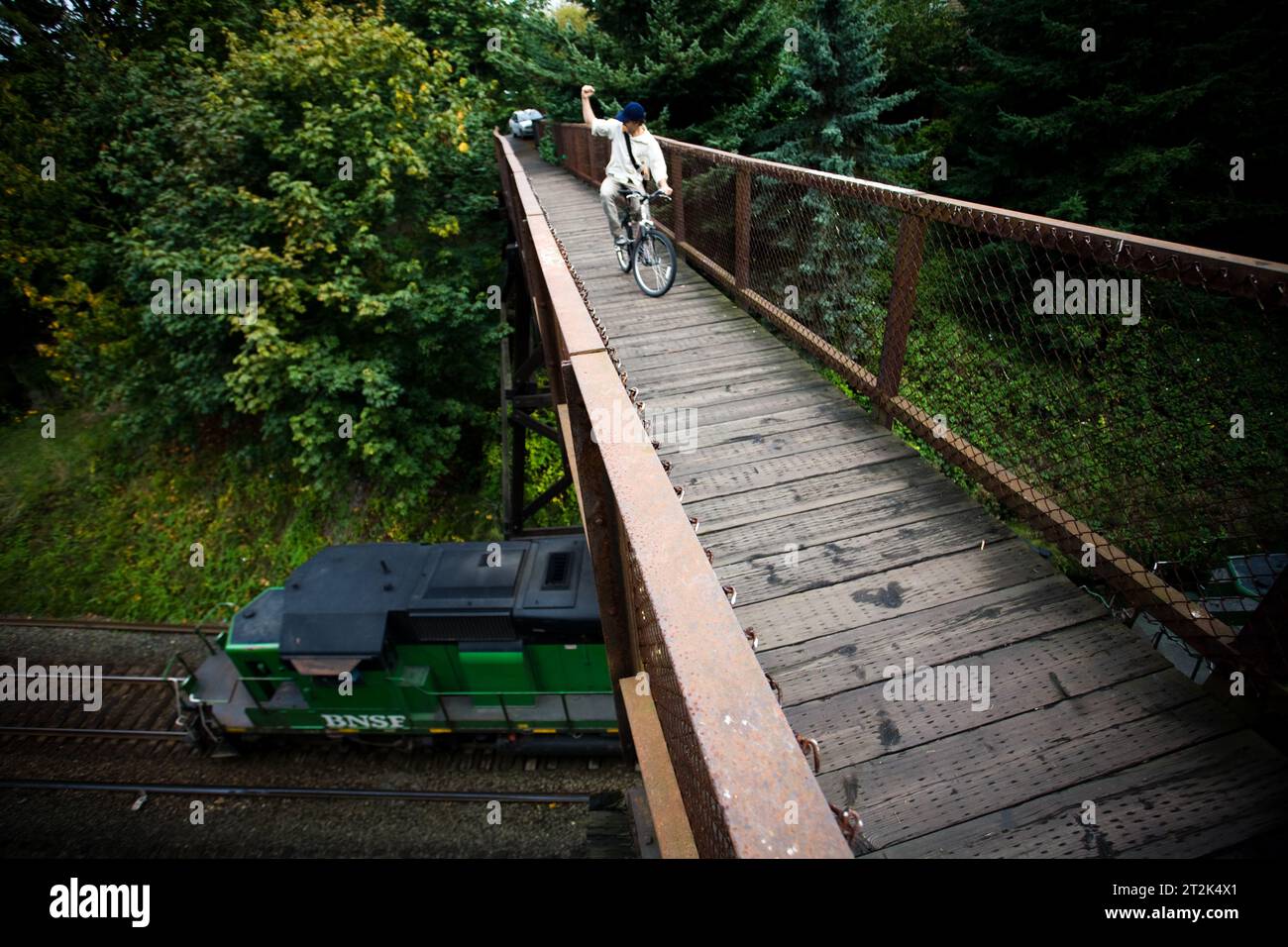 A biker crosses a bridge while signaling to a conductor on the train ...