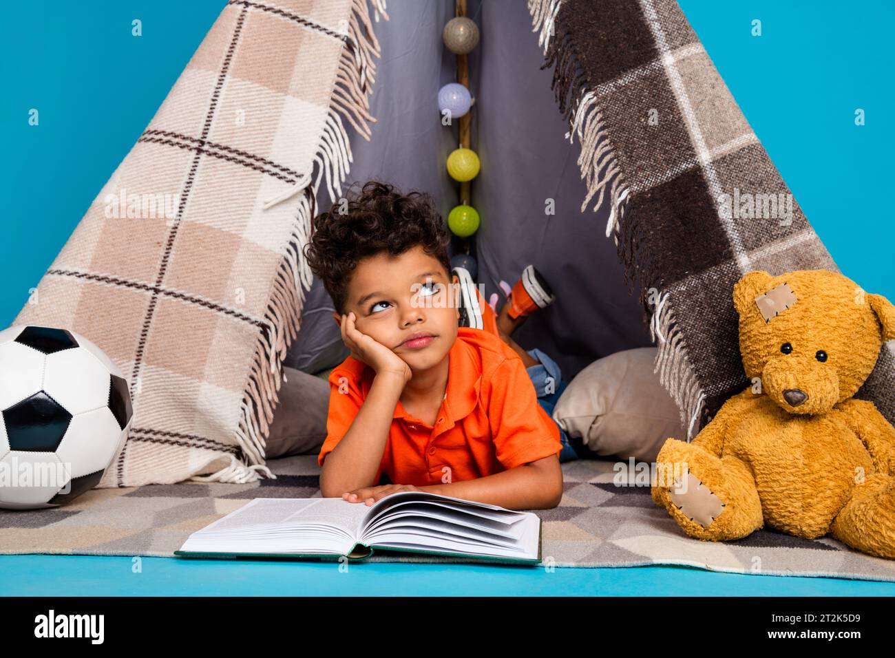 Photo of thoughtful preschool boy lying in tent tired reading learning ...