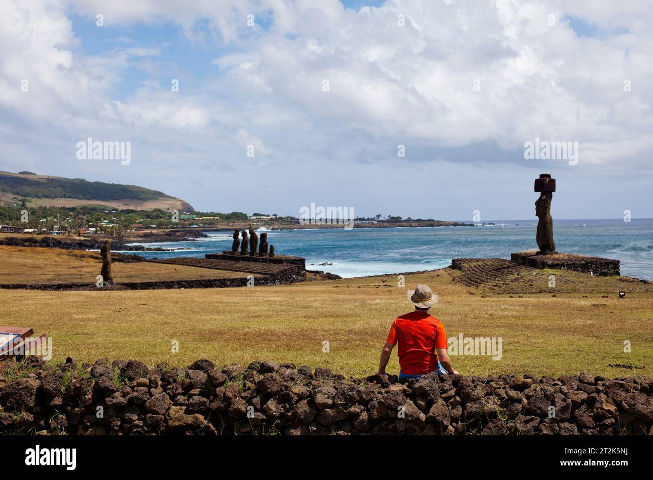A man in red sits on a rock wall overlooking the Moi and the blue water ...