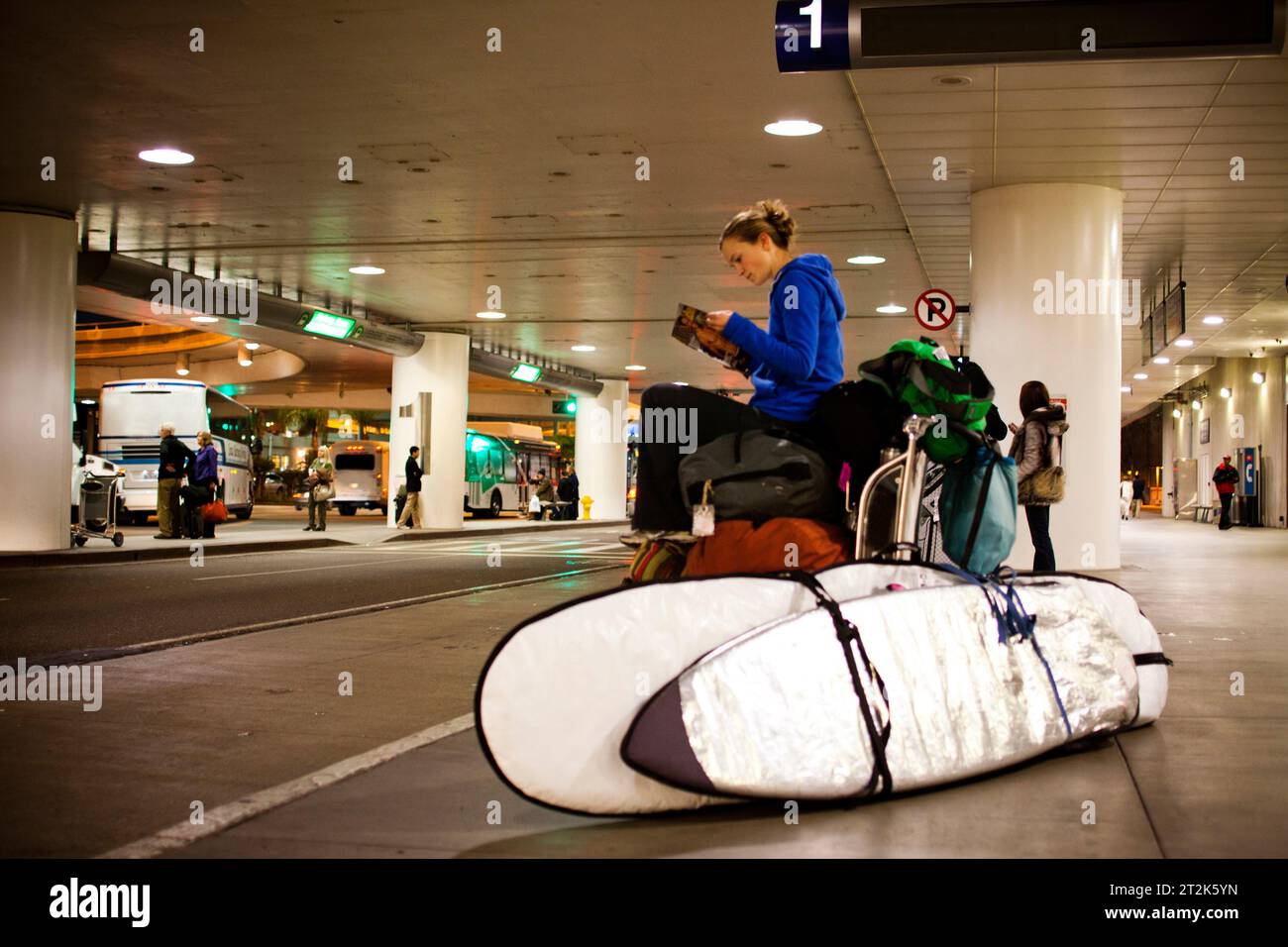 A young woman waits for an airport ride while sitting on her bags next ...