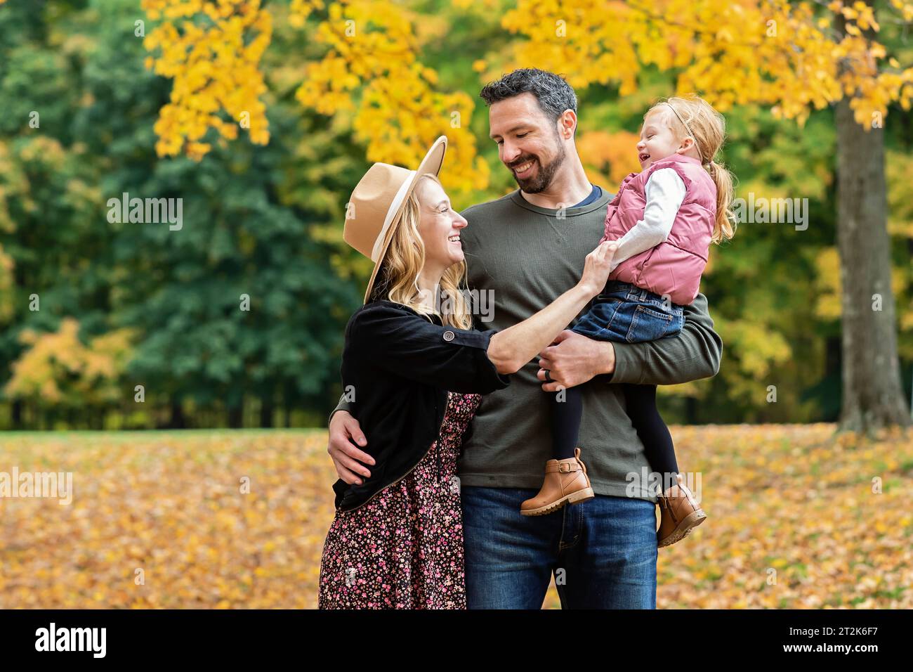 Family of three laughing and embracing amid a fall backdrop Stock Photo ...