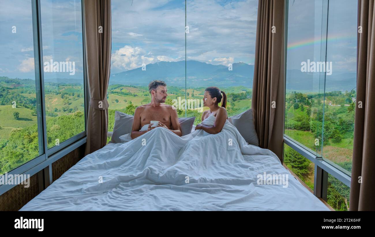 a couple of men and women laying in bed with open widows looking out ...