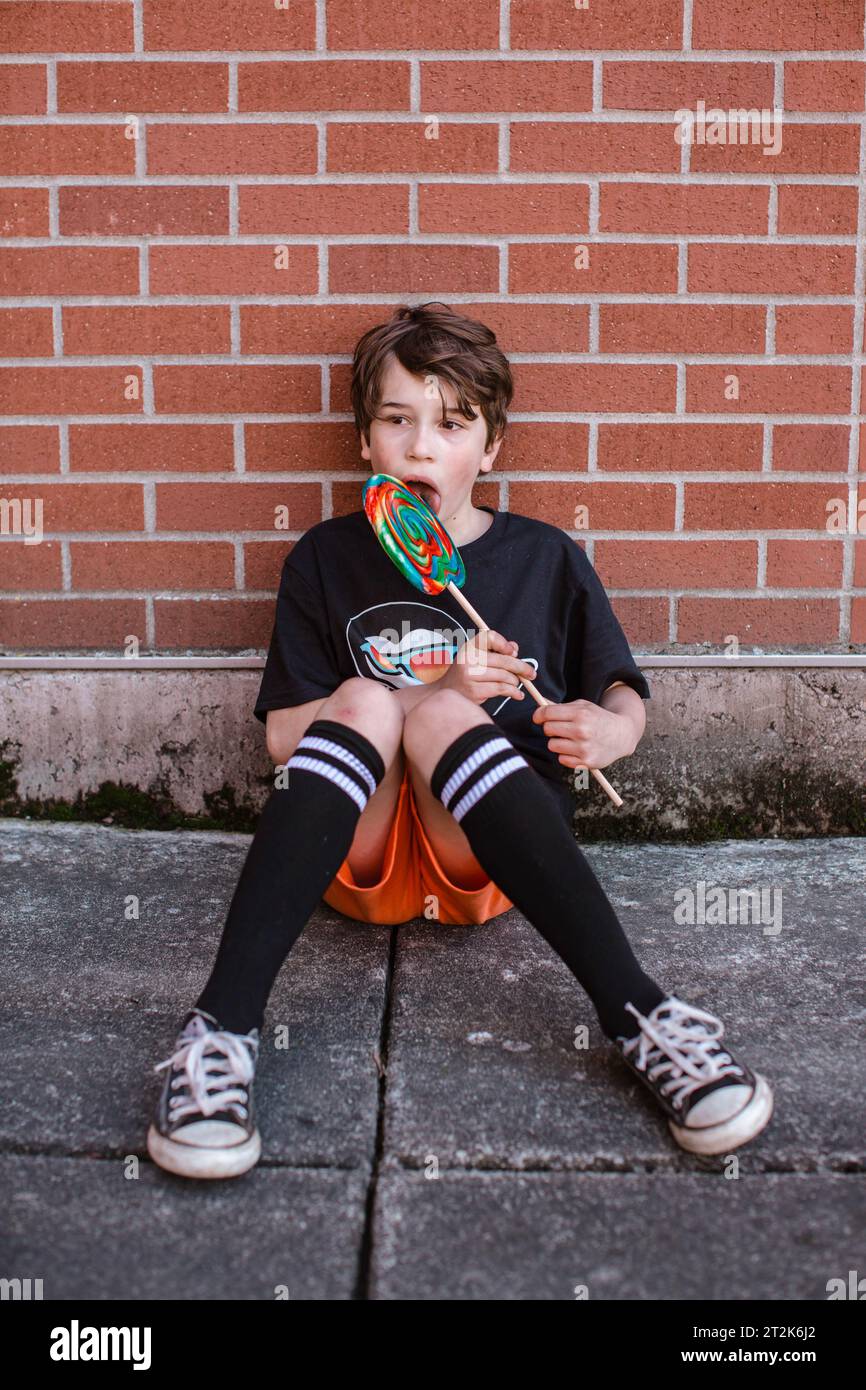 Boy Licking Rainbow Swirl Lollipop by Brick Wall Stock Photo - Alamy