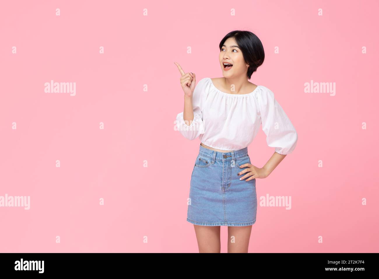 Smiling young pretty Asian woman pointing hand up and looking sideways ...