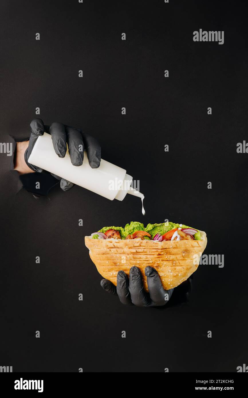 Cooks hand adding sauce to doner kebab through torn holes on black ...