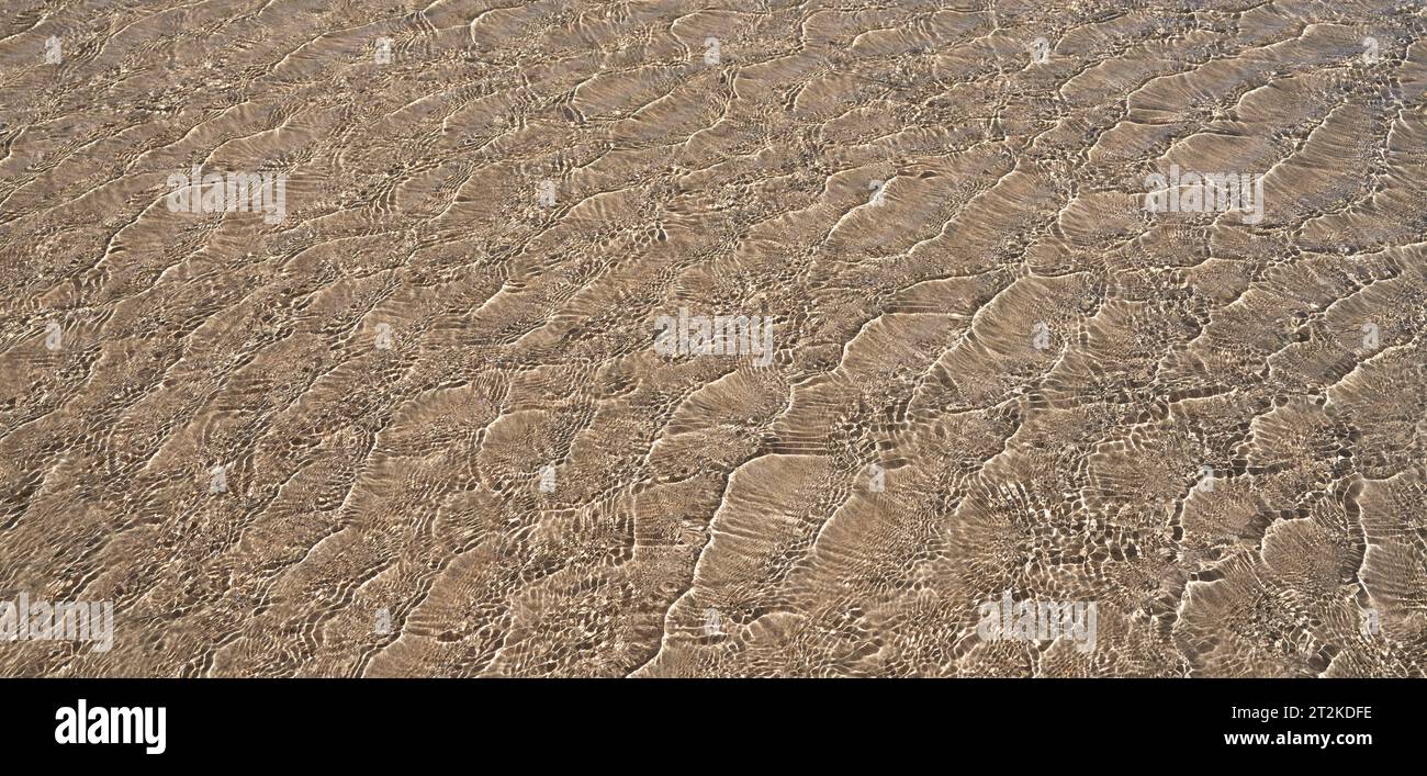 Abstract pattern in shallow clear water over brown sand on a beach ...