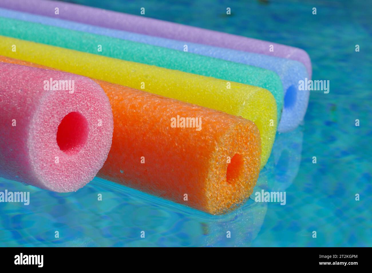 Rainbow coloured pool noodles floating in swimming pool, colourful ...