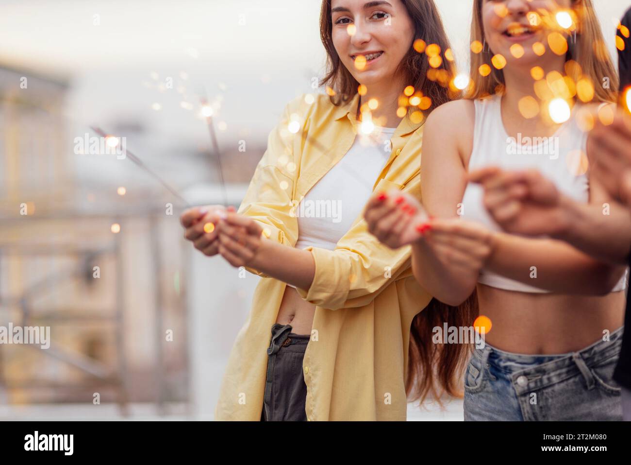 Two cute guys and two charming girls are holding sparklers and smiling ...