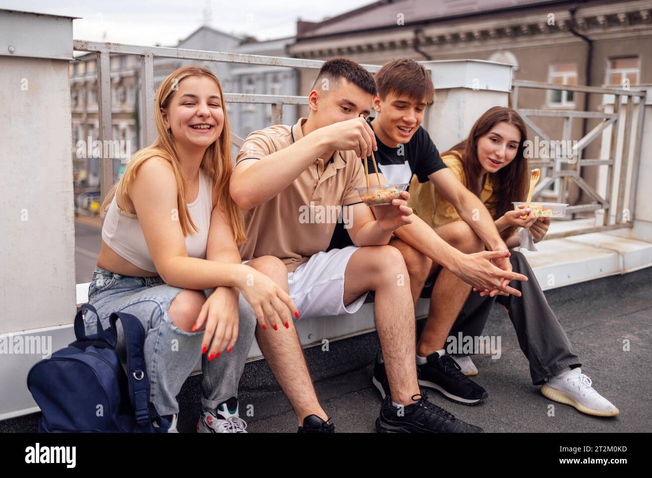 Four teenagers are sitting on the parapet on the roof of the house and ...
