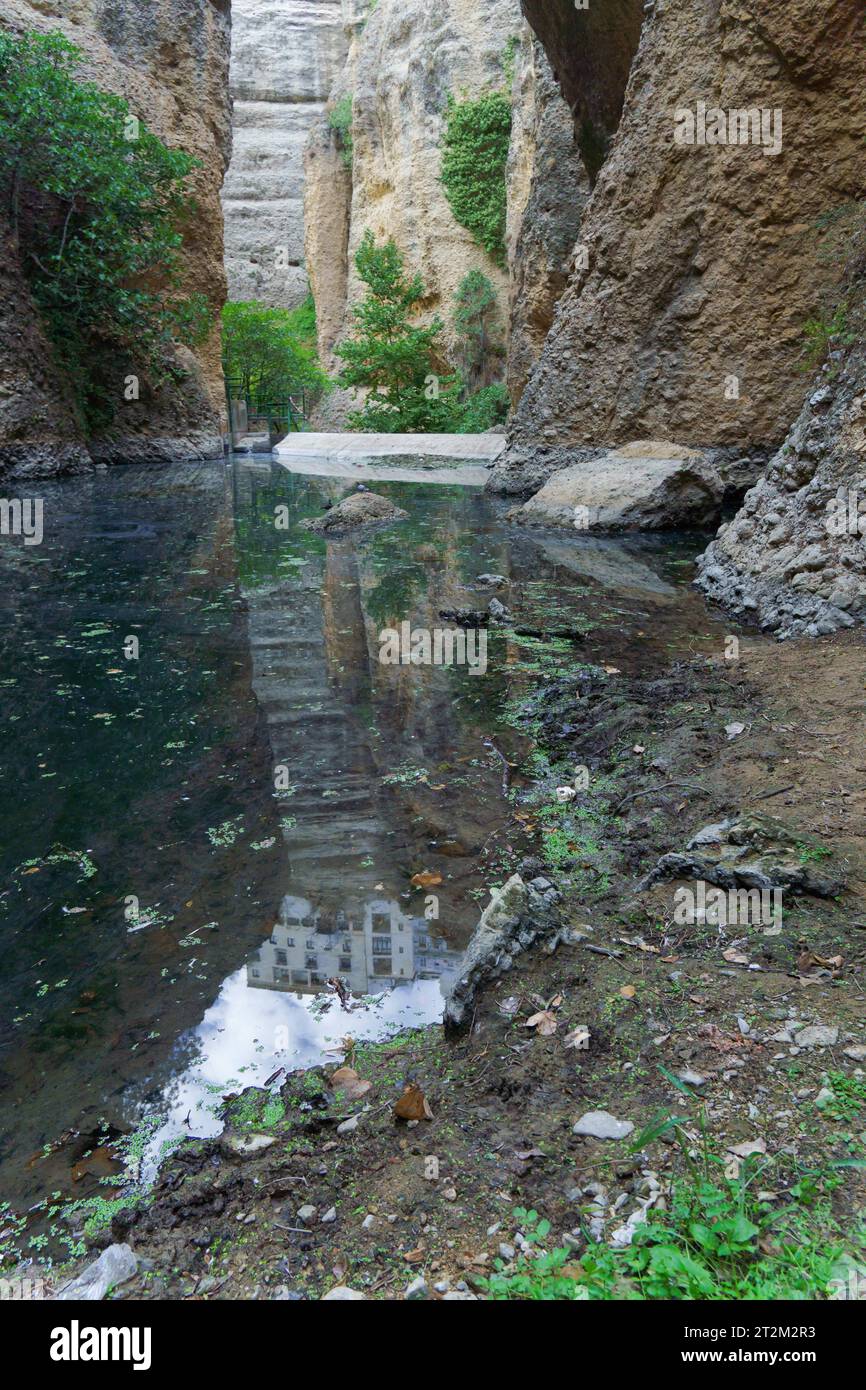 Building reflected in the waters of a river underneath a large cliff ...