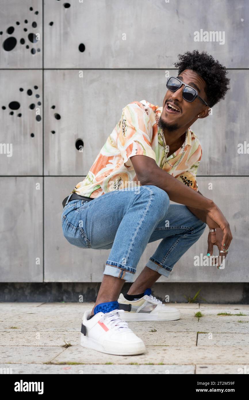 Vertical portrait of an urban afro man crouching while posing outdoors ...