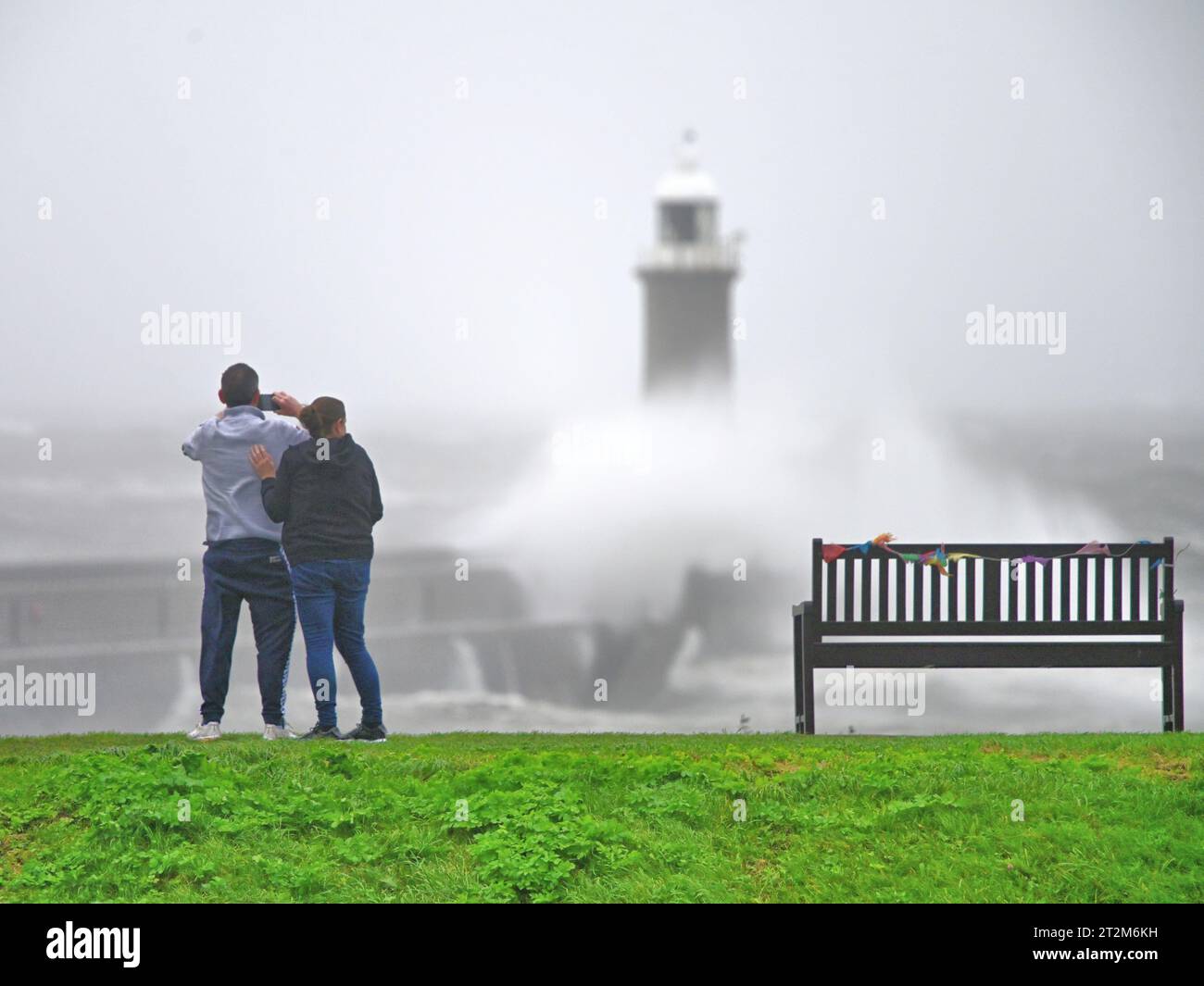 Two people watching the crashing waves on the North Pier lighthouse at ...