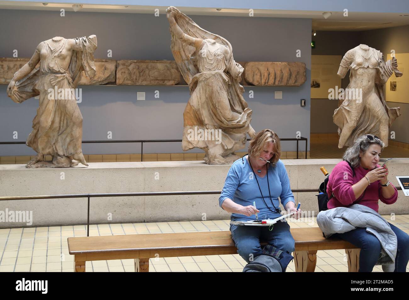 Two women sitting on a bench in front of sculptures from the Nereid ...