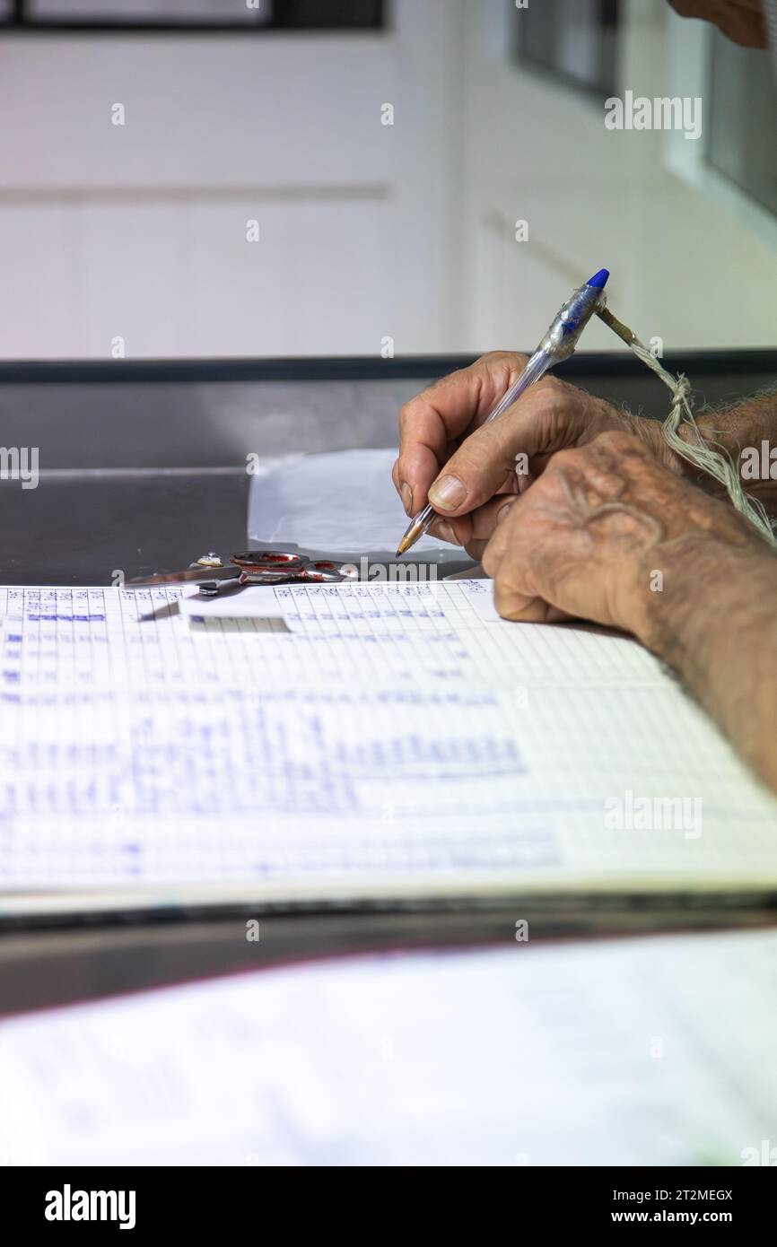 Close-up of a hand holding a pen in a book. Hand of aged man doing ...