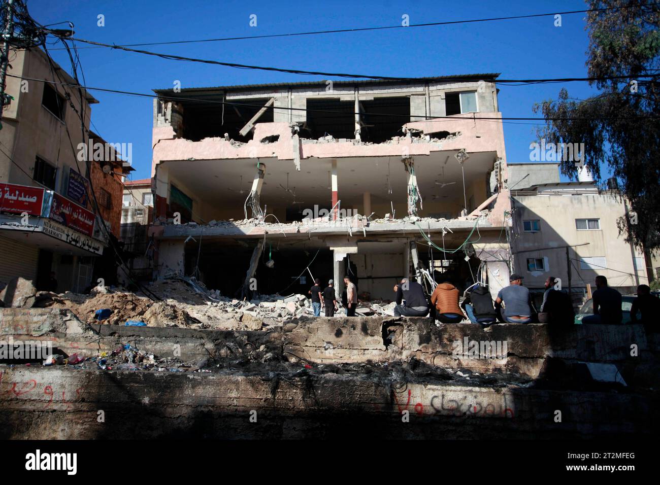 Palestinians walk next to a building damaged during a raid by Israeli ...