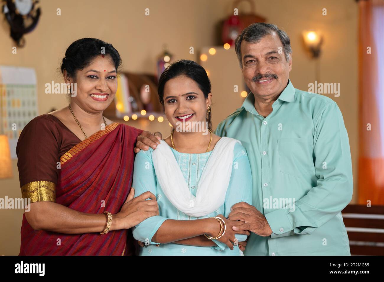 Happy smiling Indian middle class parents with daughter looking camera at home during diwali ...