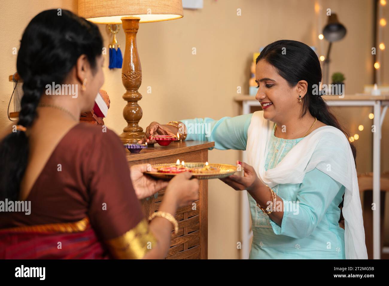Shoulder shot, joyful indian daughter with mother placing diya lamps at ...