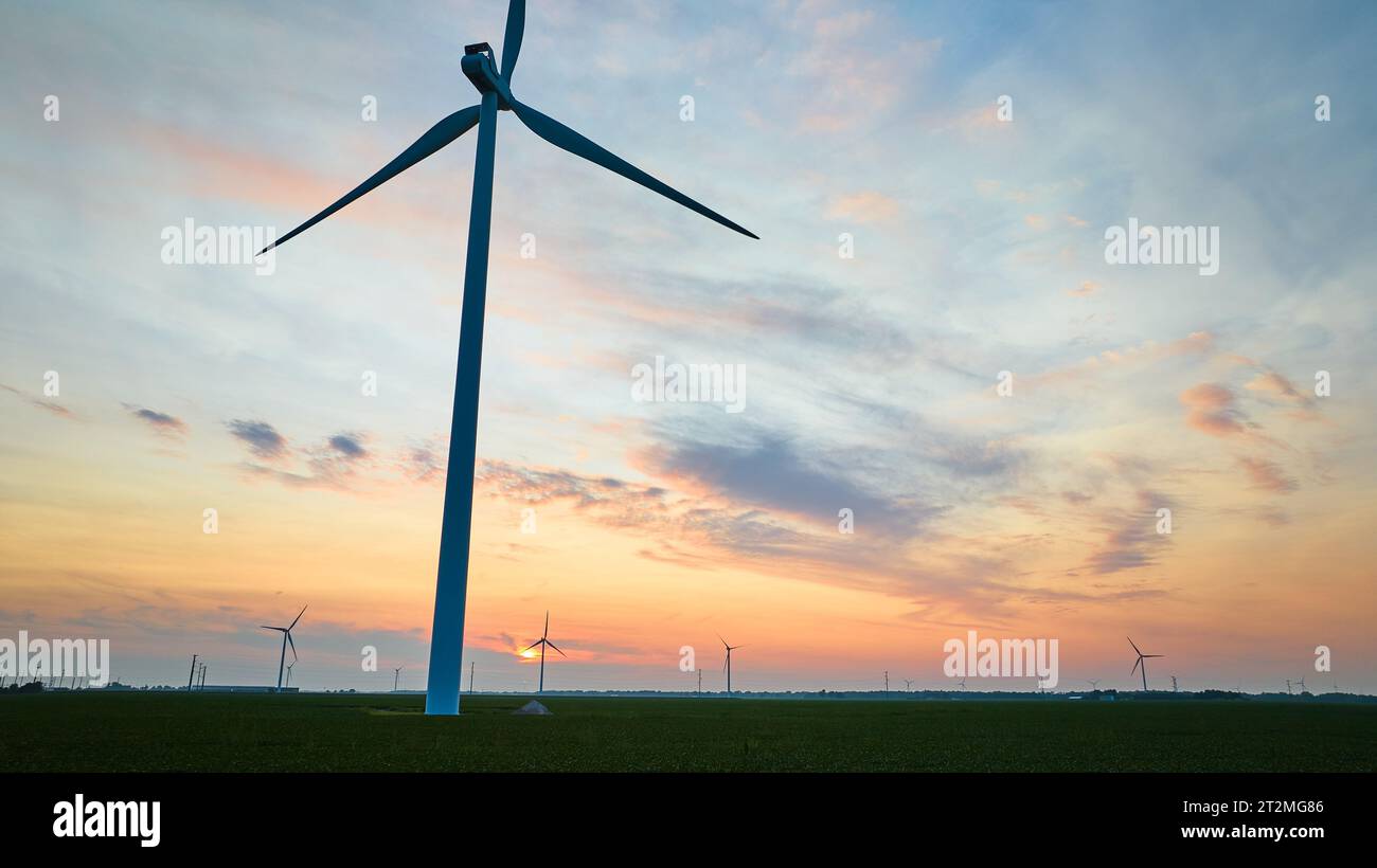 Low aerial of wind farm at sunset with pretty sky and green fields ...