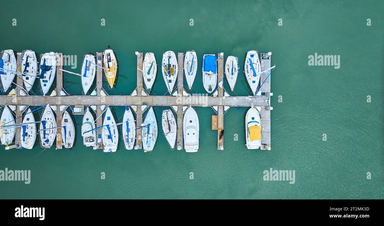 Aerial downward view of 22 boats and yachts on single pier on teal ...