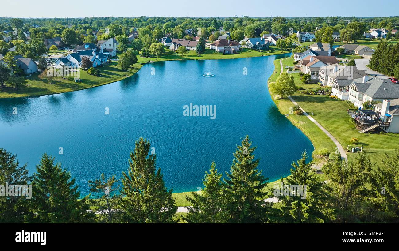 Low aerial with tree top view of large pond with water fountain and ...