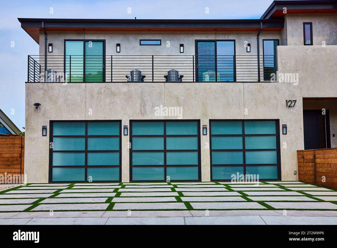 Large mansion with three garage doors and fancy balcony over grass and ...