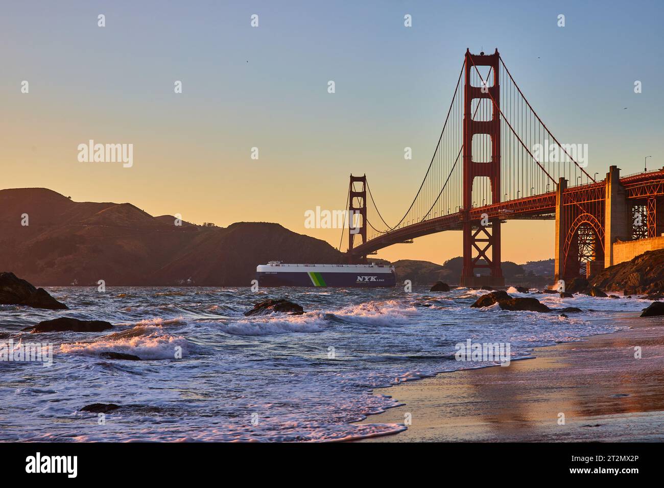 Ocean liner going under Golden Gate Bridge at sunset from sandy beach ...
