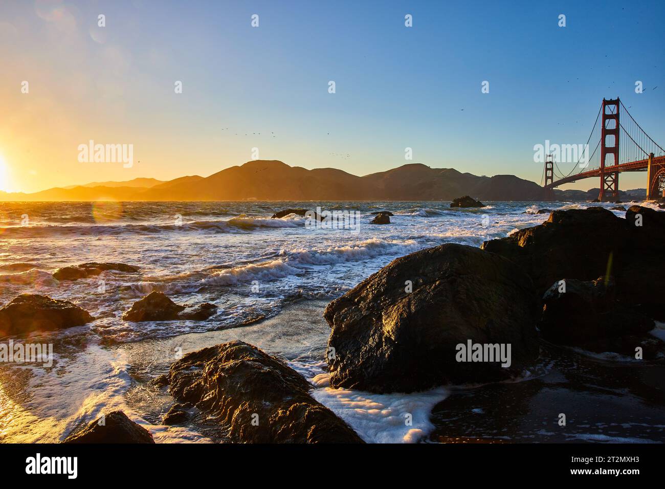 Gorgeous sunset over waves and boulders with Golden Gate Bridge and ...