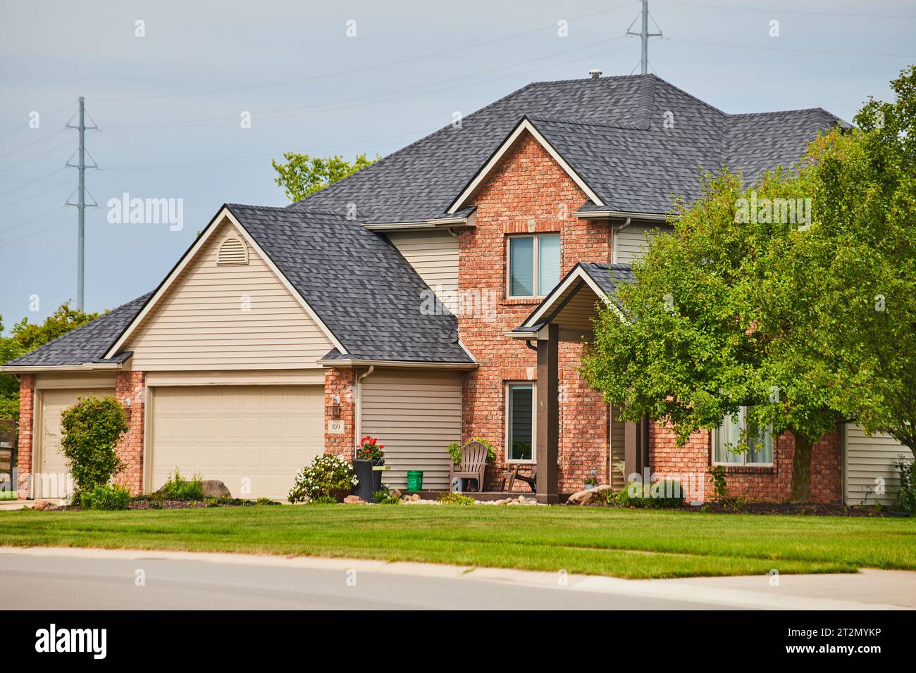 Suburban home with reddish brown brick face and overhang over front ...