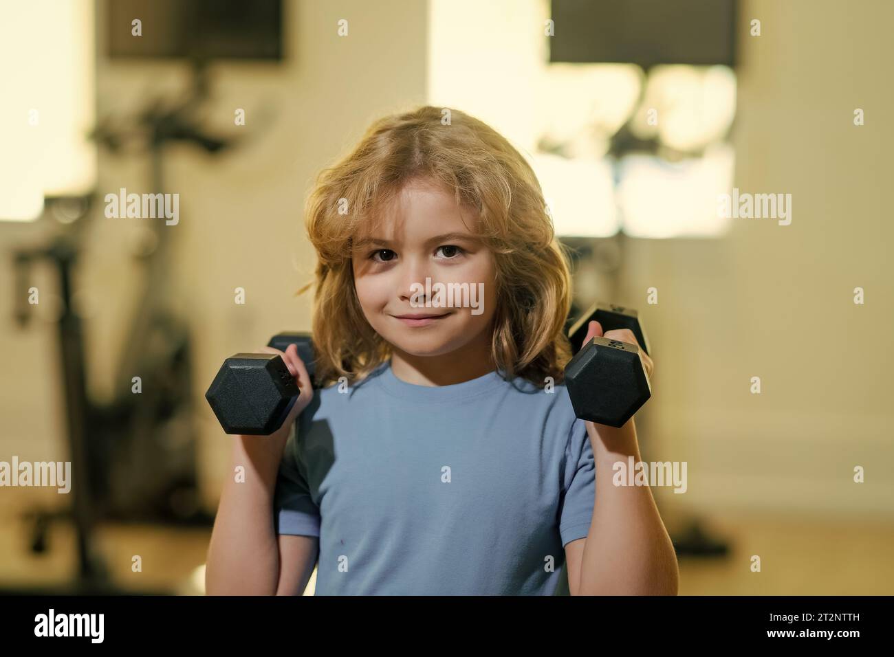 Child boy pumping up biceps muscles with dumbbell. Child workout kid in ...