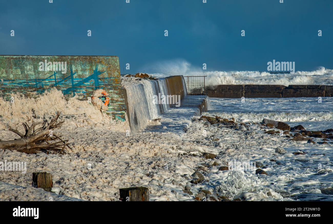 Sea foam created by very stormy waves coming over a harbour wall along ...