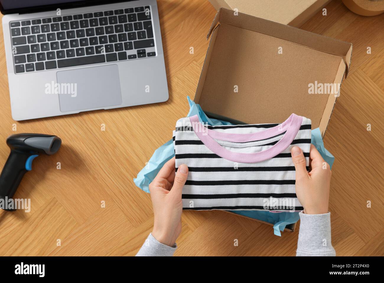 Woman packing clothes into cardboard box at wooden table, top view ...