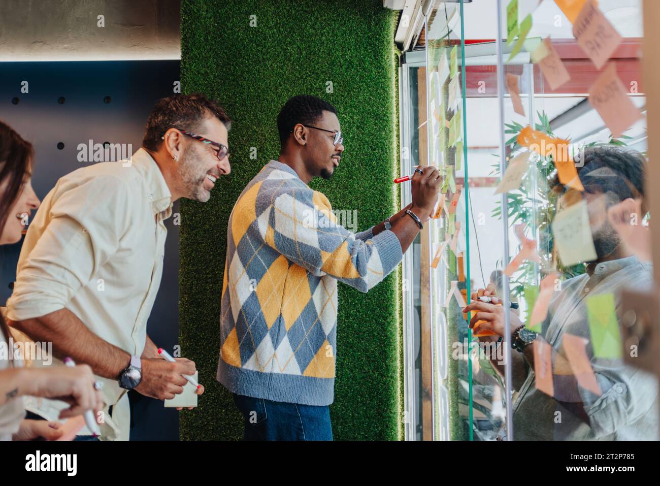 Diverse employees use sticky notes on a glass wall for creative ...