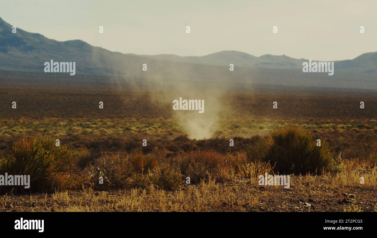In a vast and barren desert valley, a furious dust devil rips, tears ...