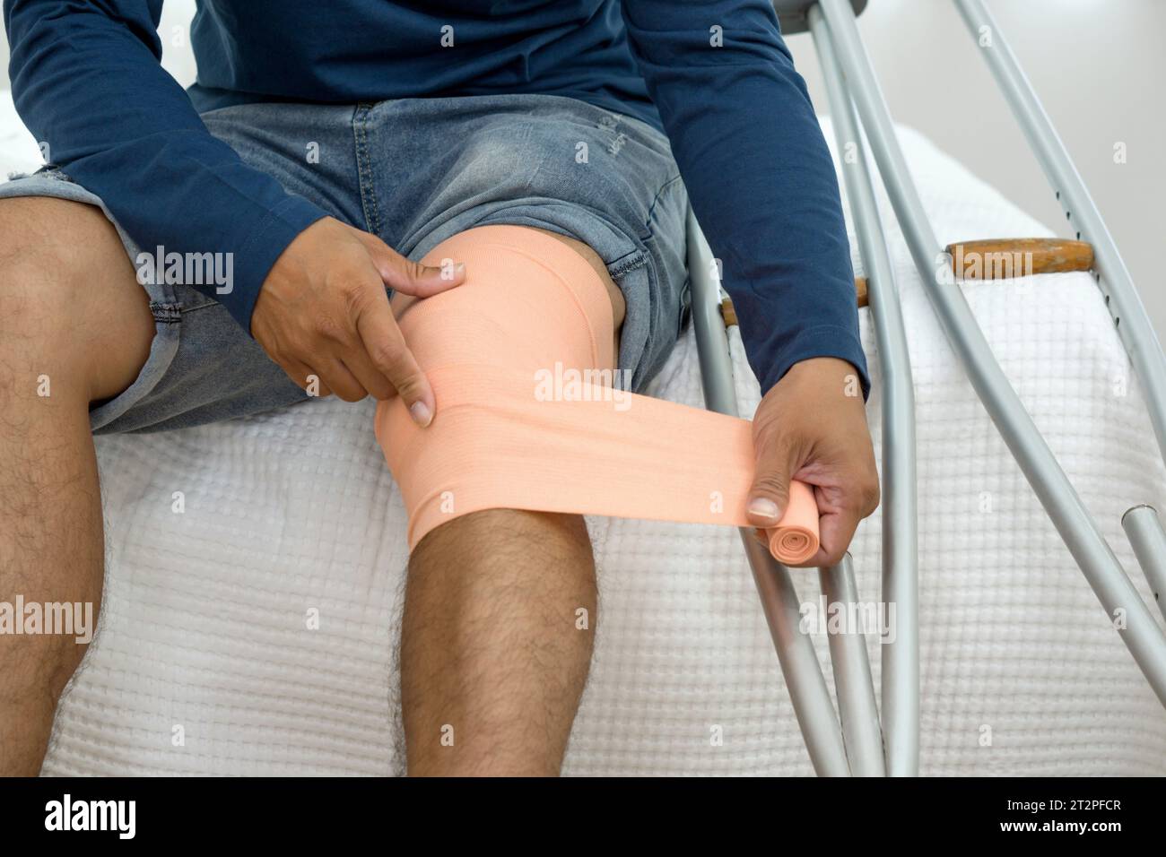 A man with a broken knee sitting on his bed. He leans on crutches ...