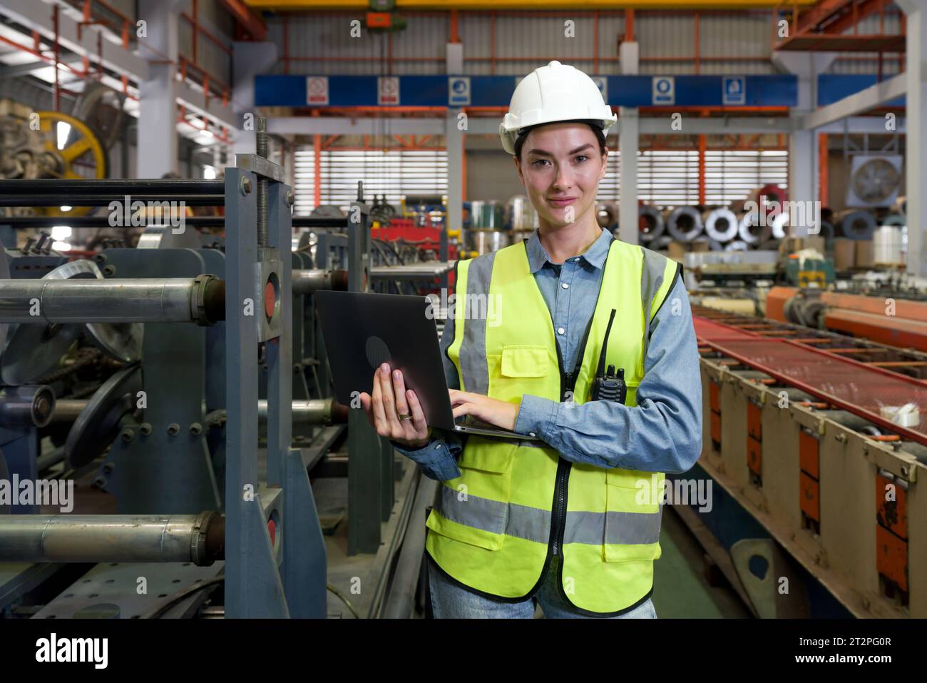 A dedicated female engineer dressed in safety gear, holding laptop ...