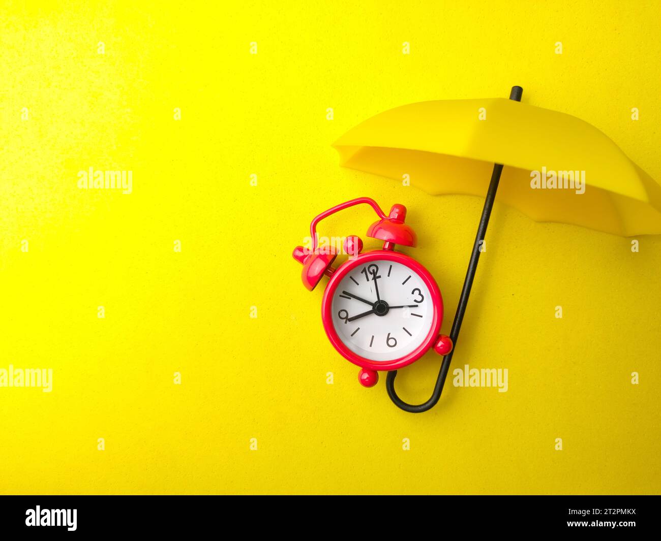 A red alarm clock with yellow umbrella on a yellow background with copy ...