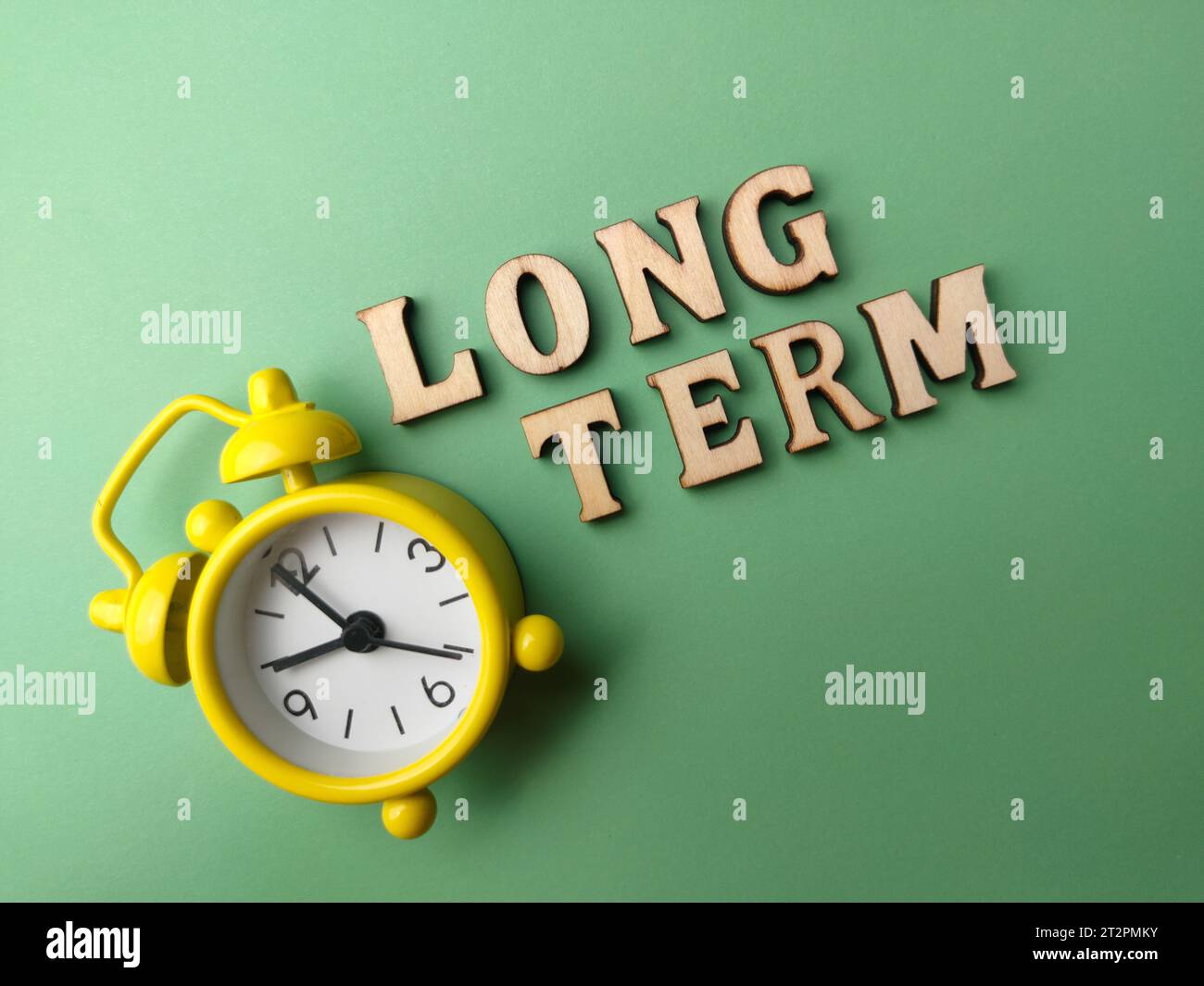 Top view wooden word and clock with word Long Term on green background ...
