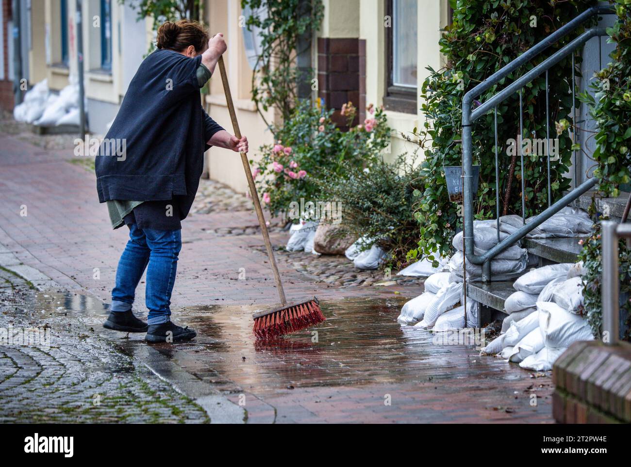 Wismar, Germany. 21st Oct, 2023. A shopkeeper sweeps water from the ...