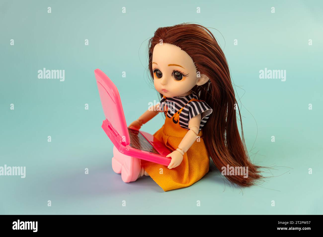 A child toy doll with dark hair in an orange dress standing on a blue ...