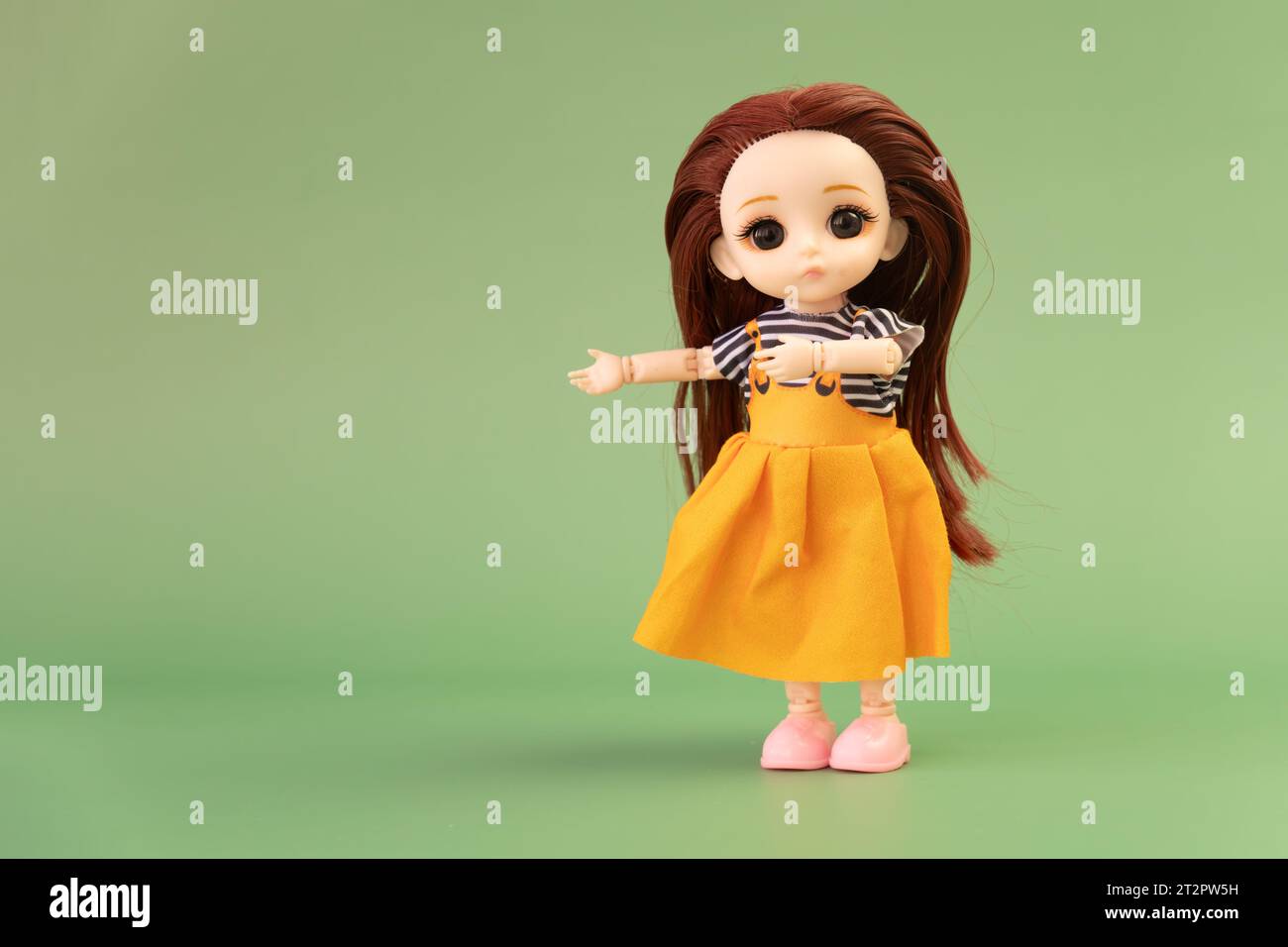A child toy doll with dark hair in an orange dress standing on a green ...