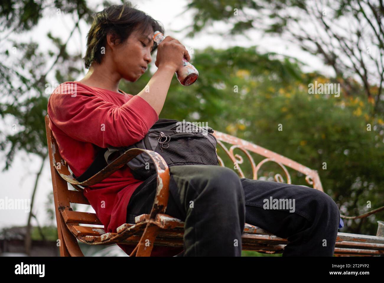 Javanese man in red shirt, sitting on a bench, plant background with a ...