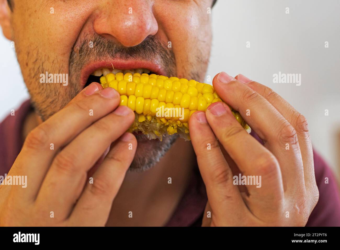 man bites off a piece of sweet corn with his teeth Stock Photo - Alamy