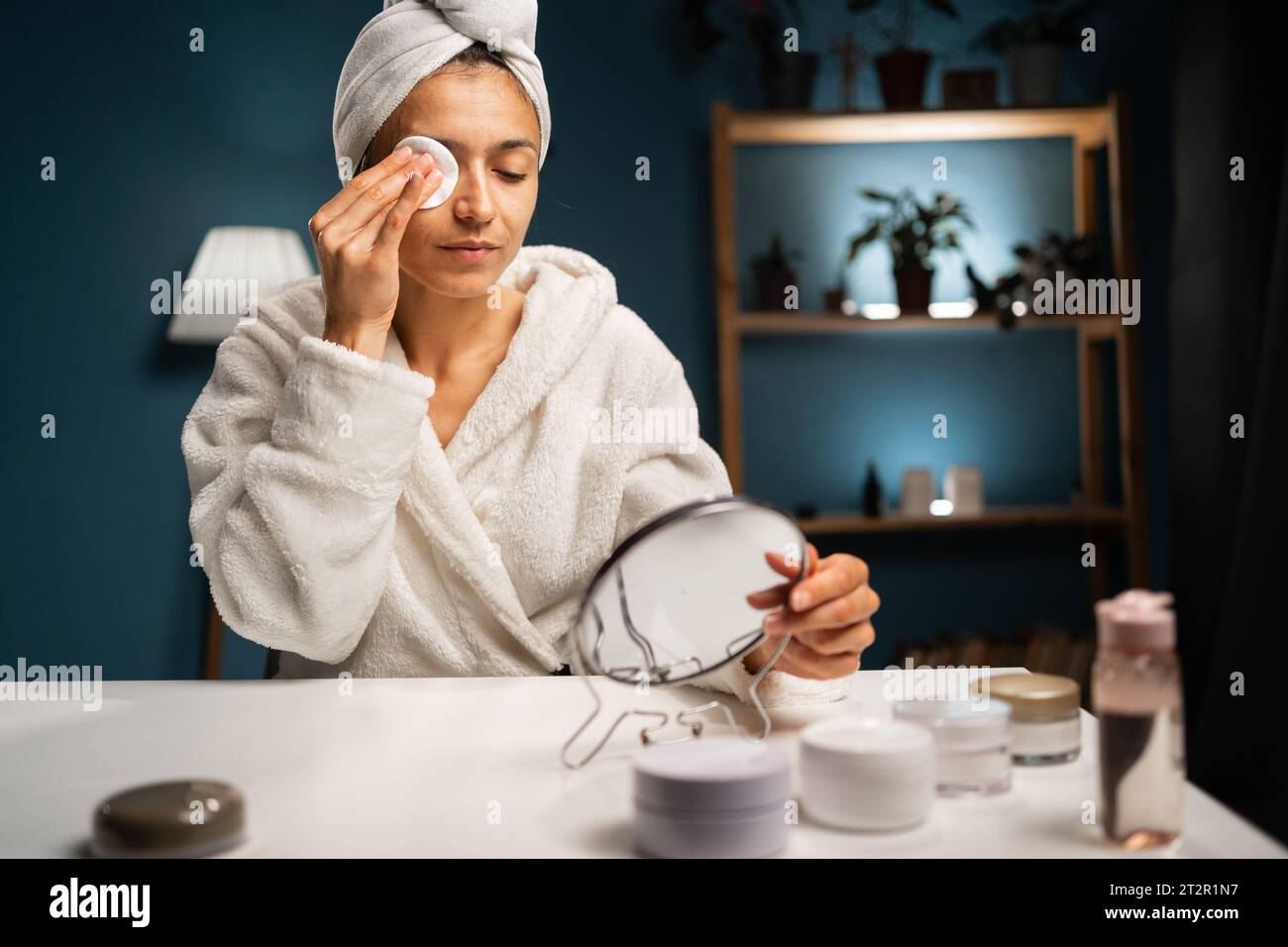 Cute woman cleaning face with cosmetic cotton pad in home interior ...