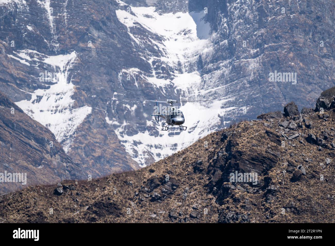 A helicopter skimming over a mountain ridge in the Himalayan Mountains ...
