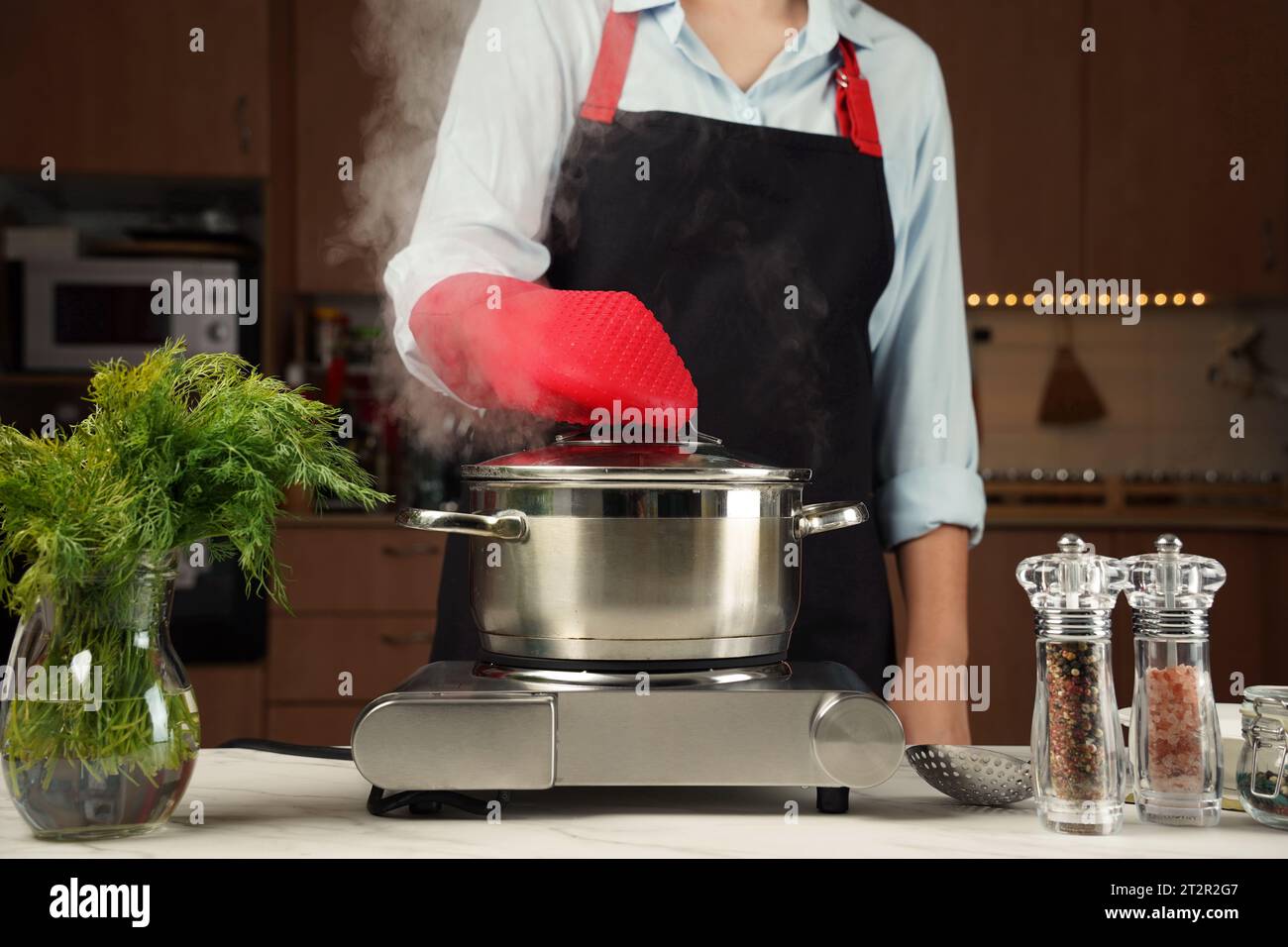 Female hand open lid of steel cooking pan on electric hob with boiling ...