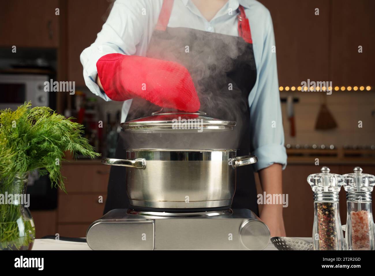 Female hand open lid of steel cooking pan on electric hob with boiling ...