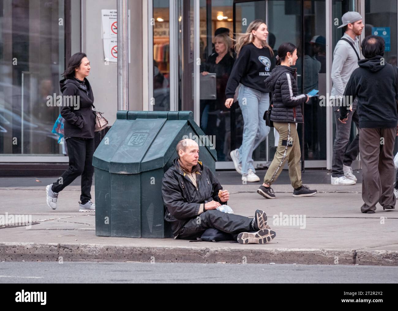 Toronto, Canada, a man sits in the sidewalk while eating a snack ...